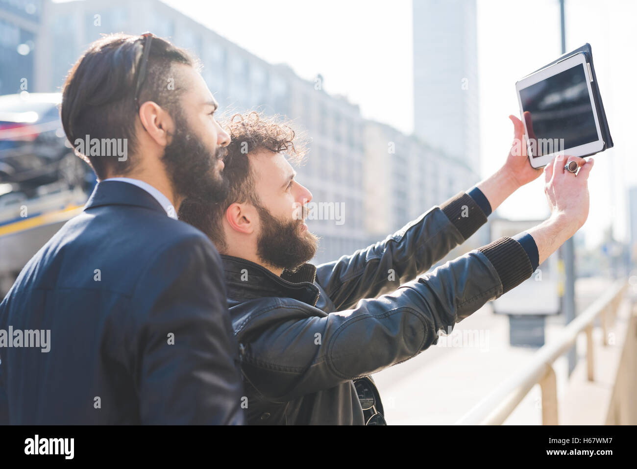 Two young bearded man outdoor in the city holding tablet, taking selfie ...