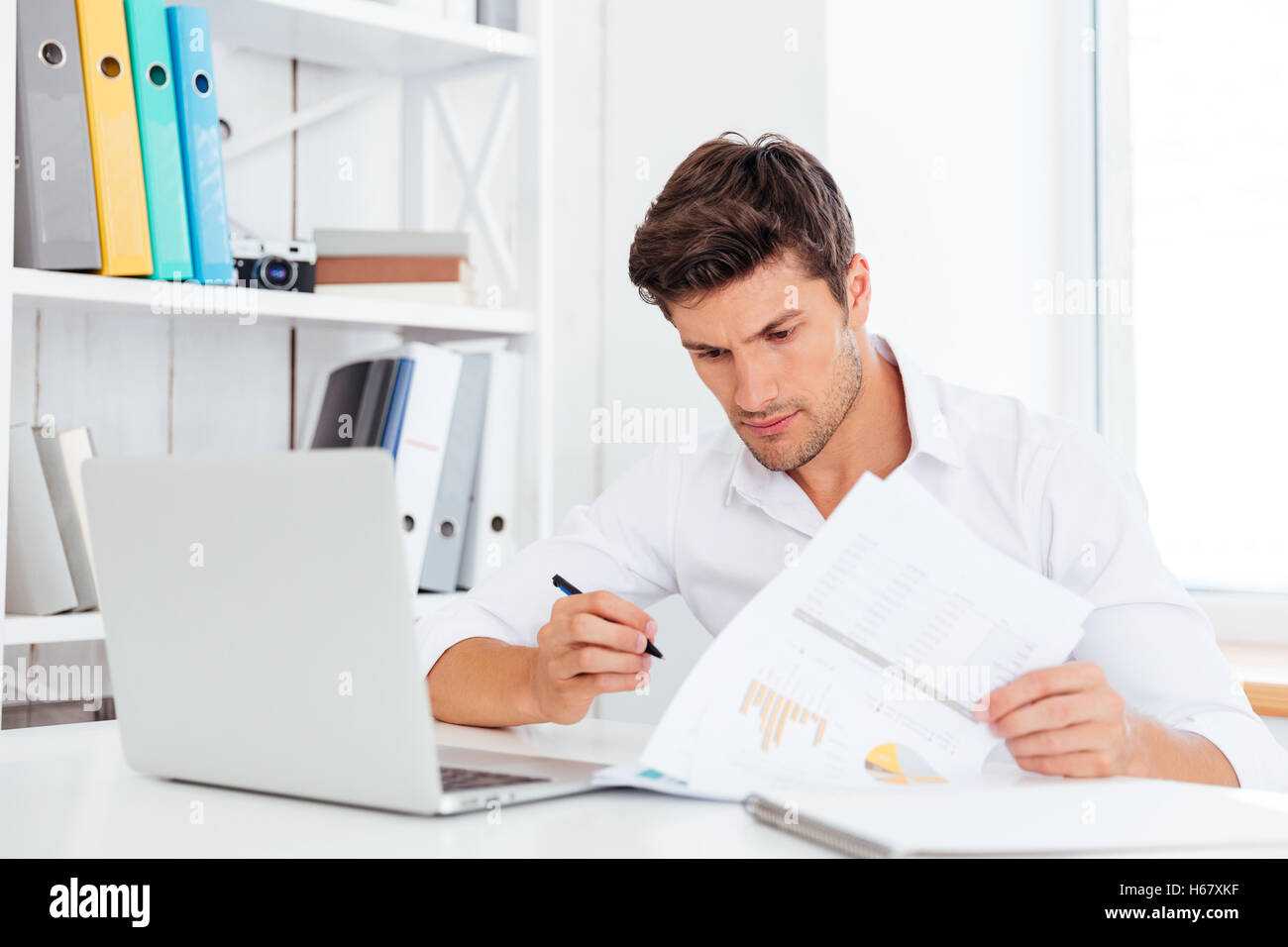 Concentrated young businessman sitting and writing at the table in ...