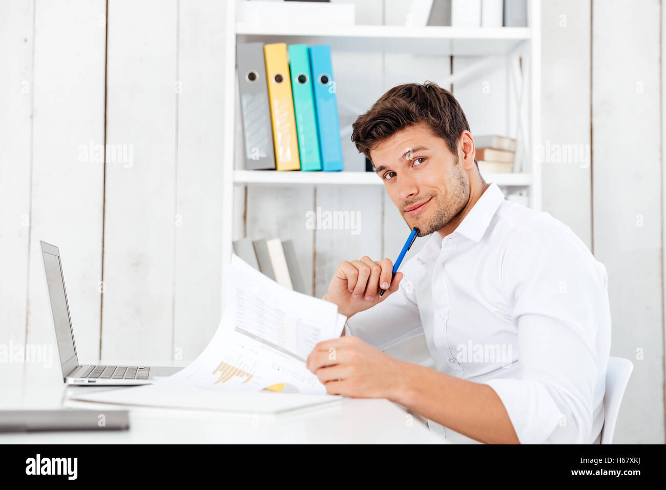 Smiling young businessman signing documents and looking at camera in ...