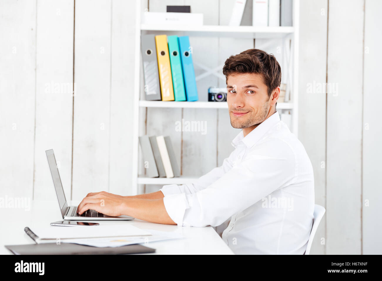 Side view of handsome young smiling businessman in casual cloth sitting ...