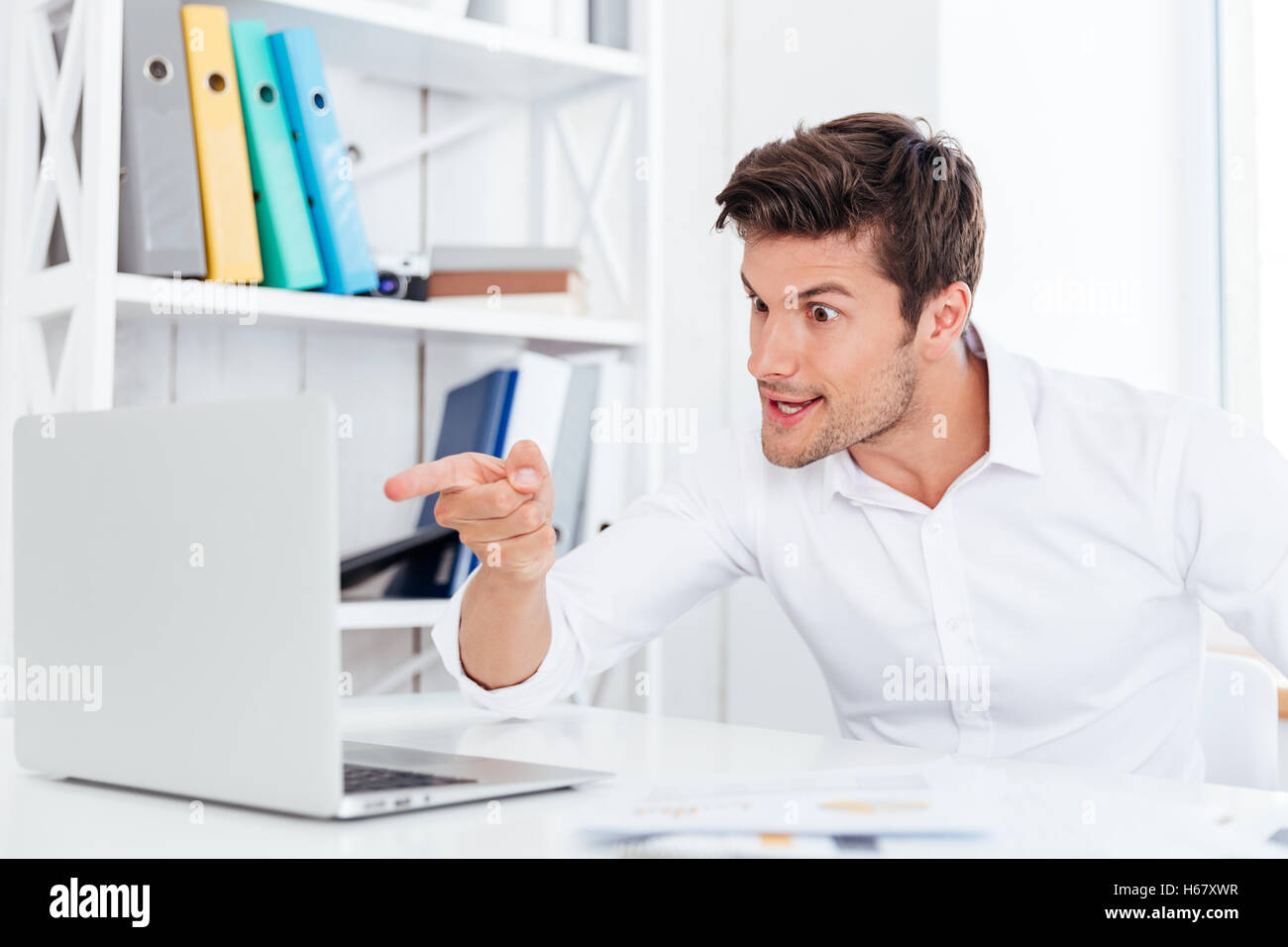 Angry annoyed businessman pointing finger at laptop while sitting at ...