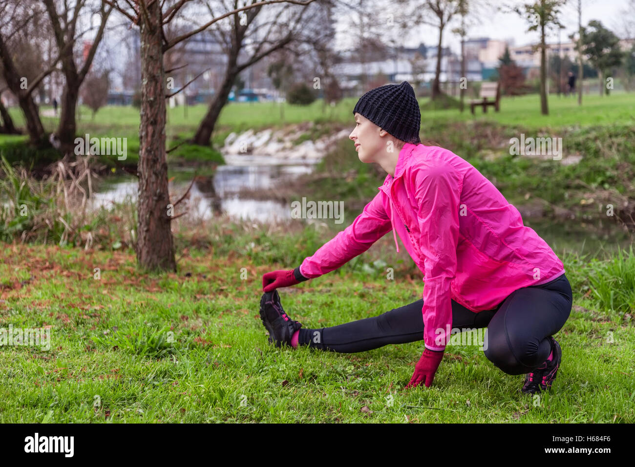 Young woman warming up and stretching the legs before running on a cold ...