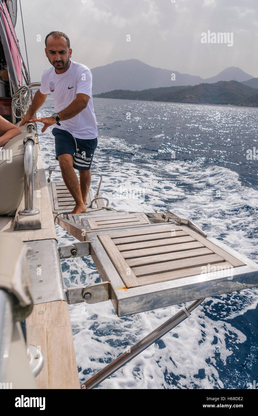 A crewmember prepares to lower a wooden gangway from the side of a ship ...