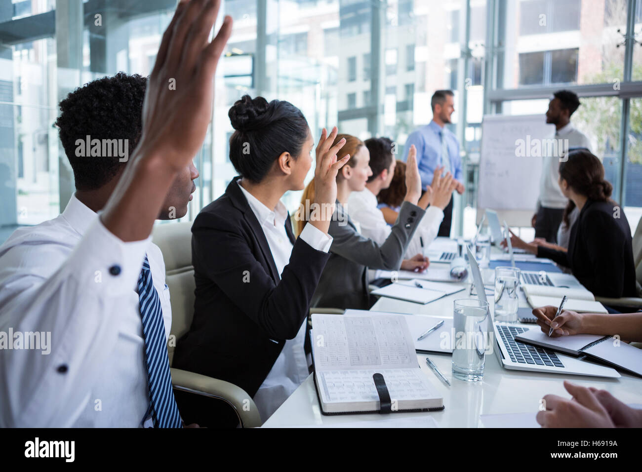Colleagues raising their hands during meeting Stock Photo - Alamy