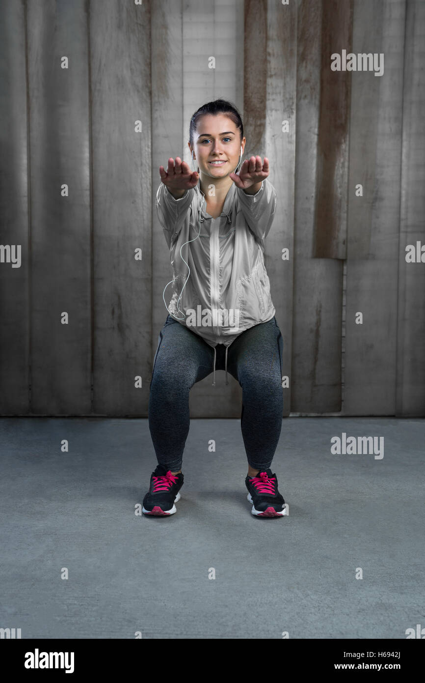 Deep squat. Front view of young beautiful woman in sportswear doing ...