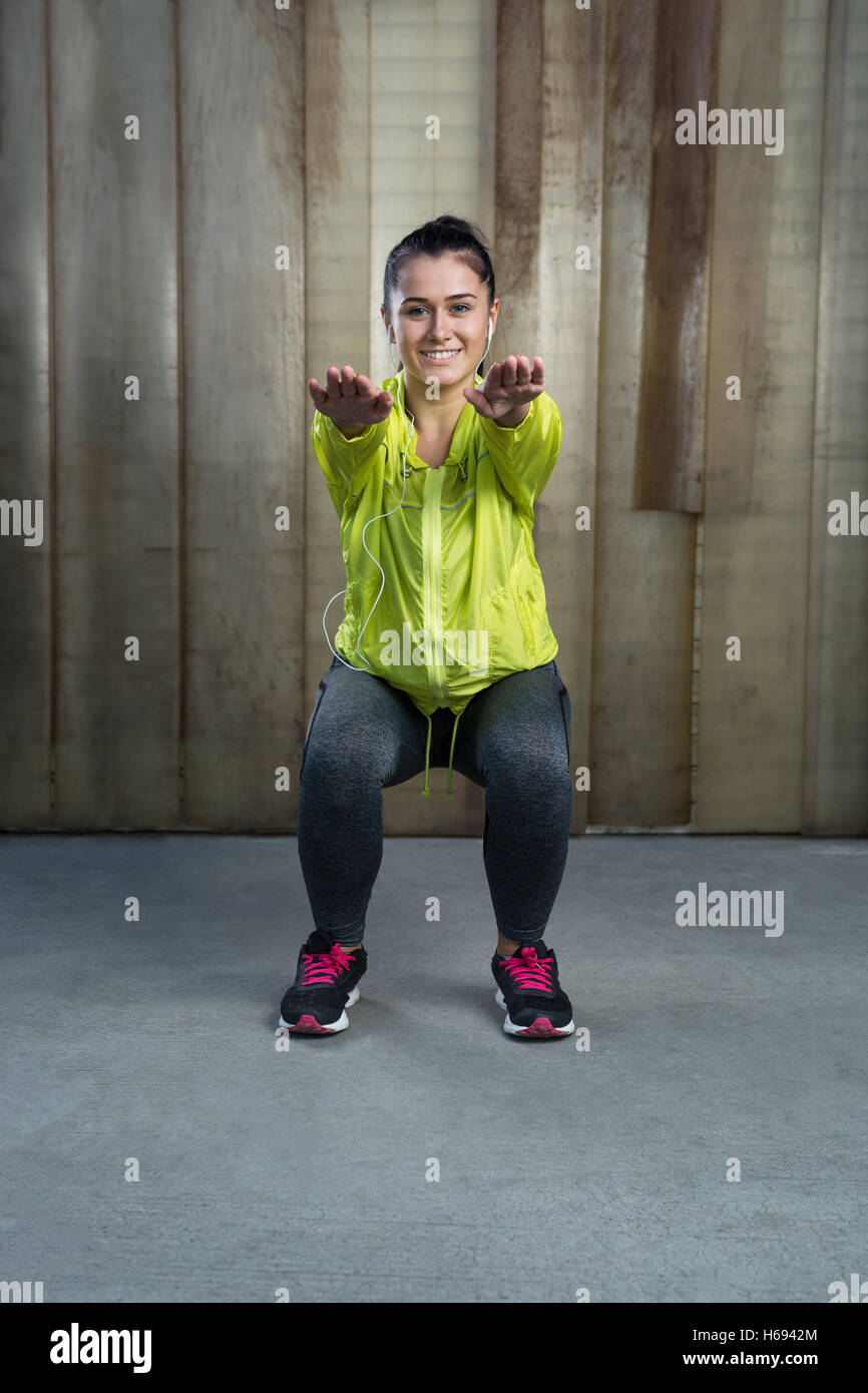 Deep squat. Front view of young beautiful woman in sportswear doing ...