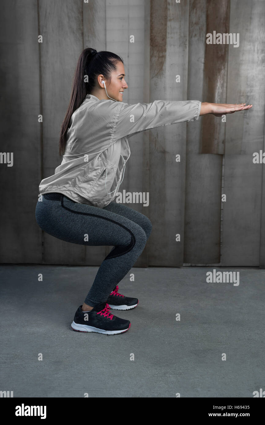 Deep squat. Side view of young beautiful woman in sportswear doing ...