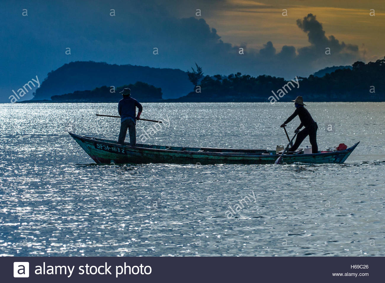 Two fishermen are silhouetted as they man their boat Stock Photo - Alamy