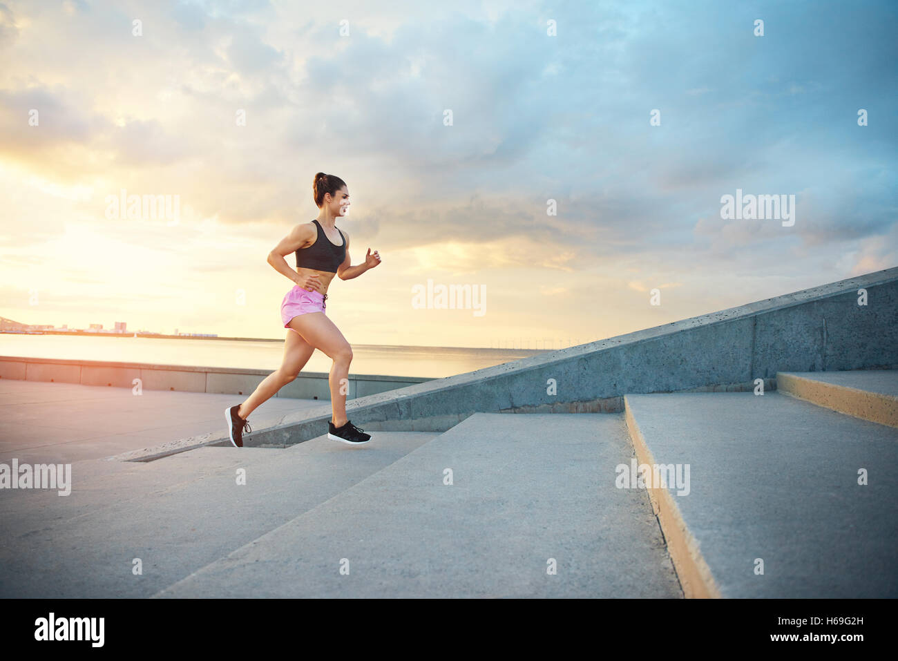 Young woman training on a morning run mounting a set of concrete steps ...