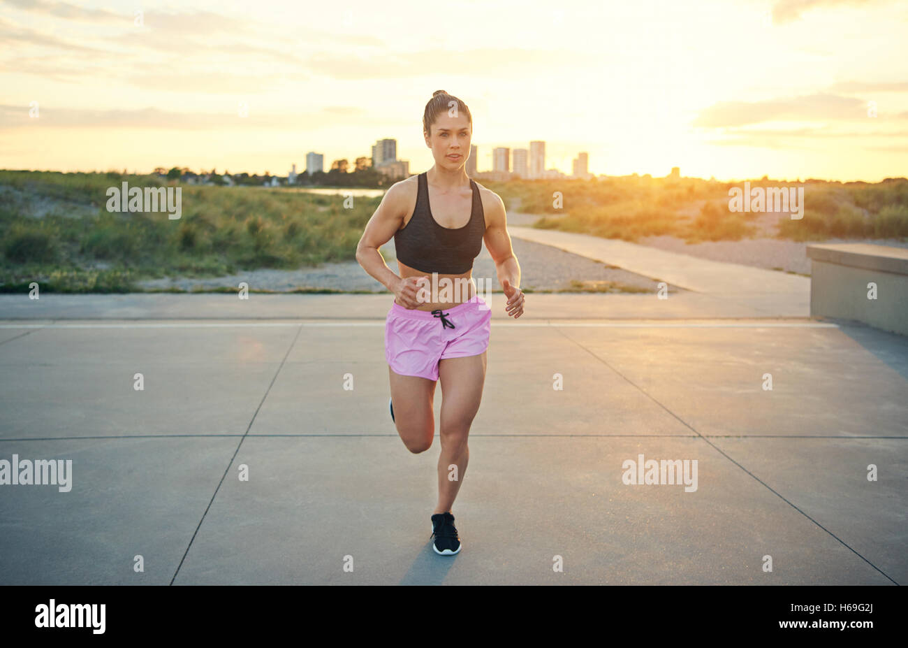 Muscular active woman working out running across a cement forecourt ...