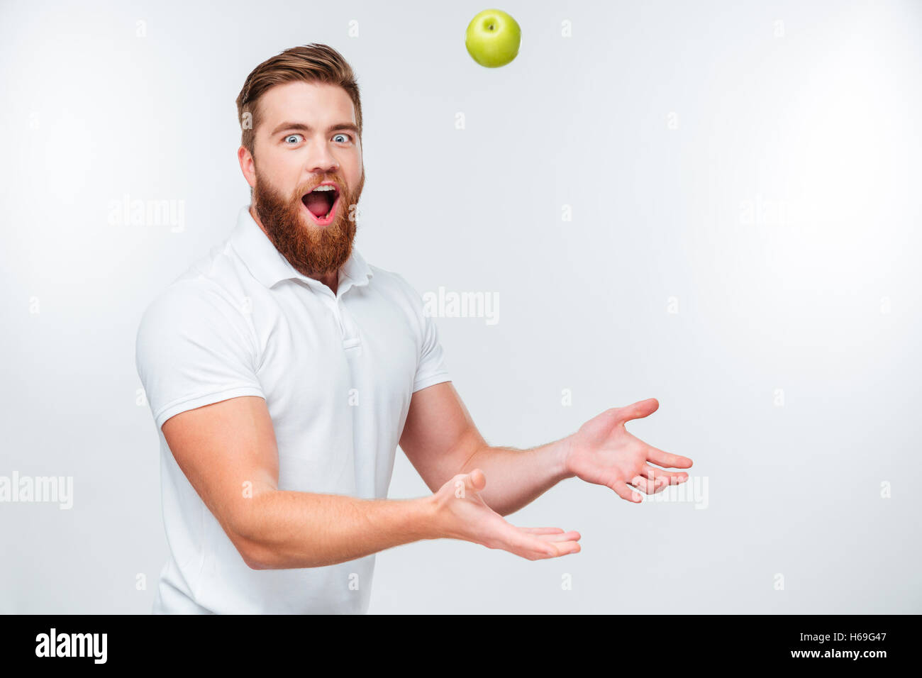 Portrait of handsome funny bearded man throwing apple up isolated on ...