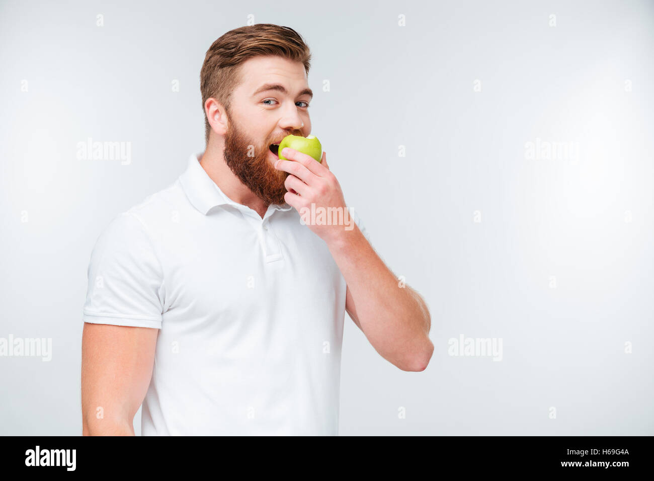 Cheerful young man is eating apple isolated over white background Stock ...