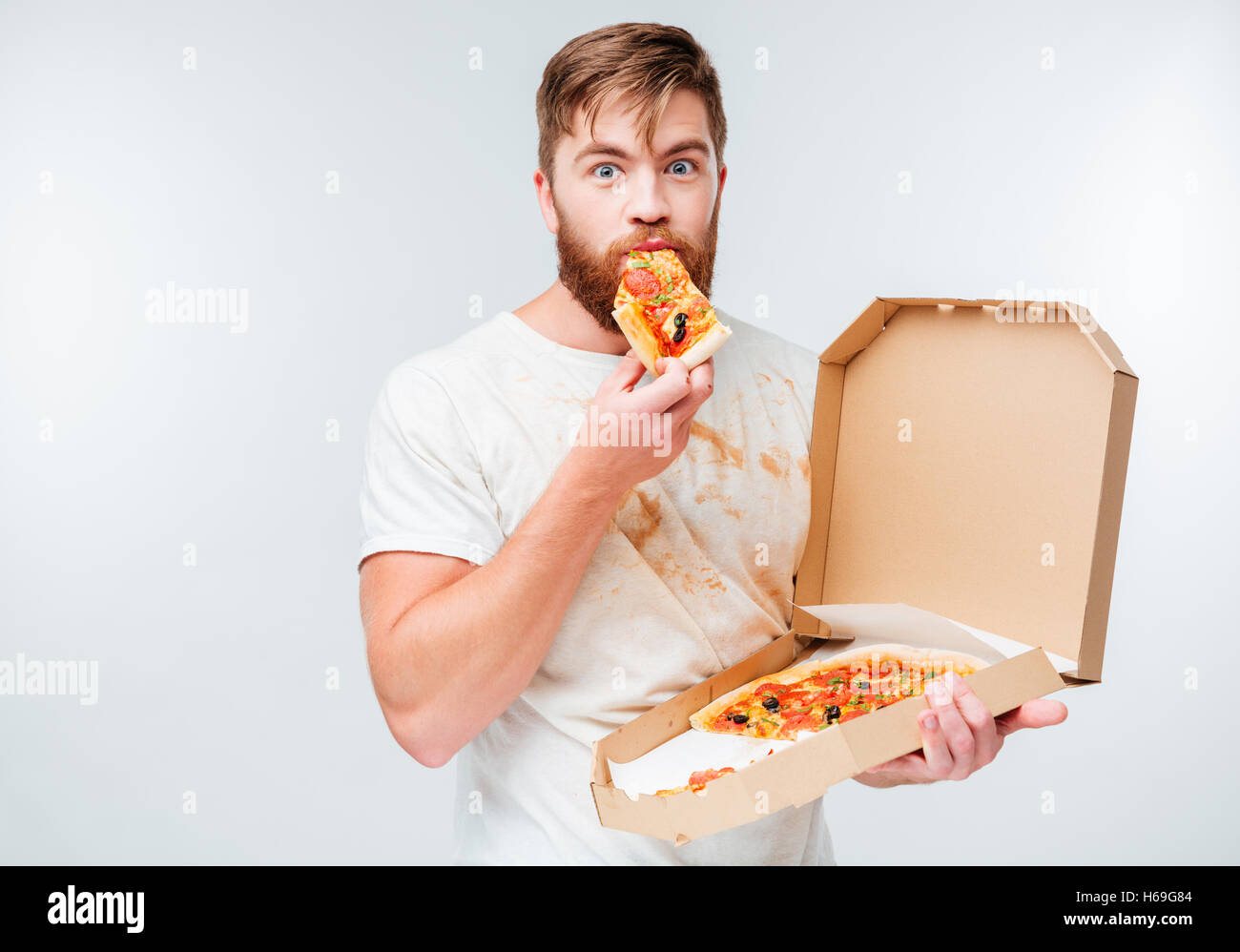 Happy hungry man eating pizza from a box isolated on white background ...
