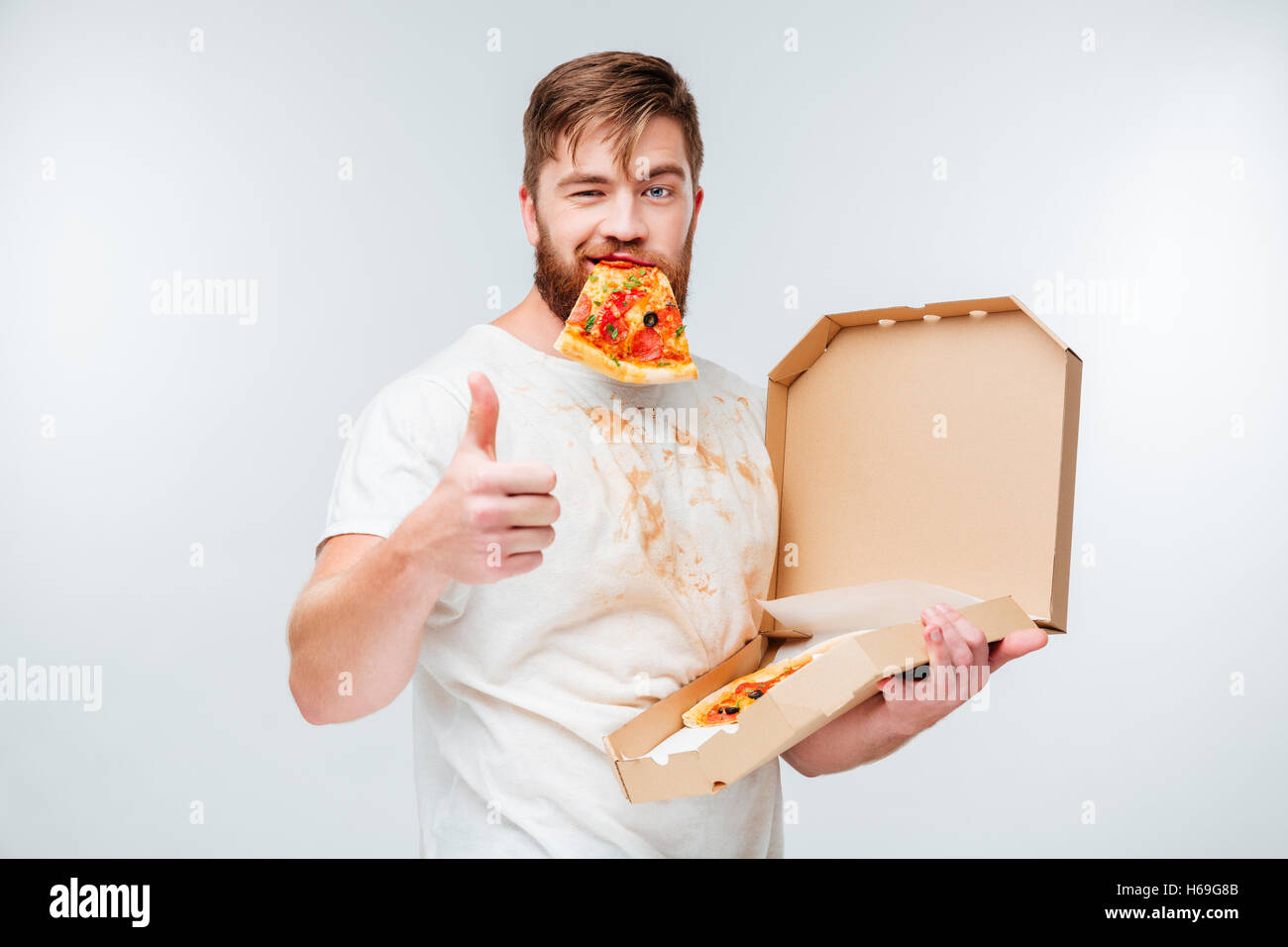 Happy hungry man eating pizza and showing thumbs up gesture isolated on ...