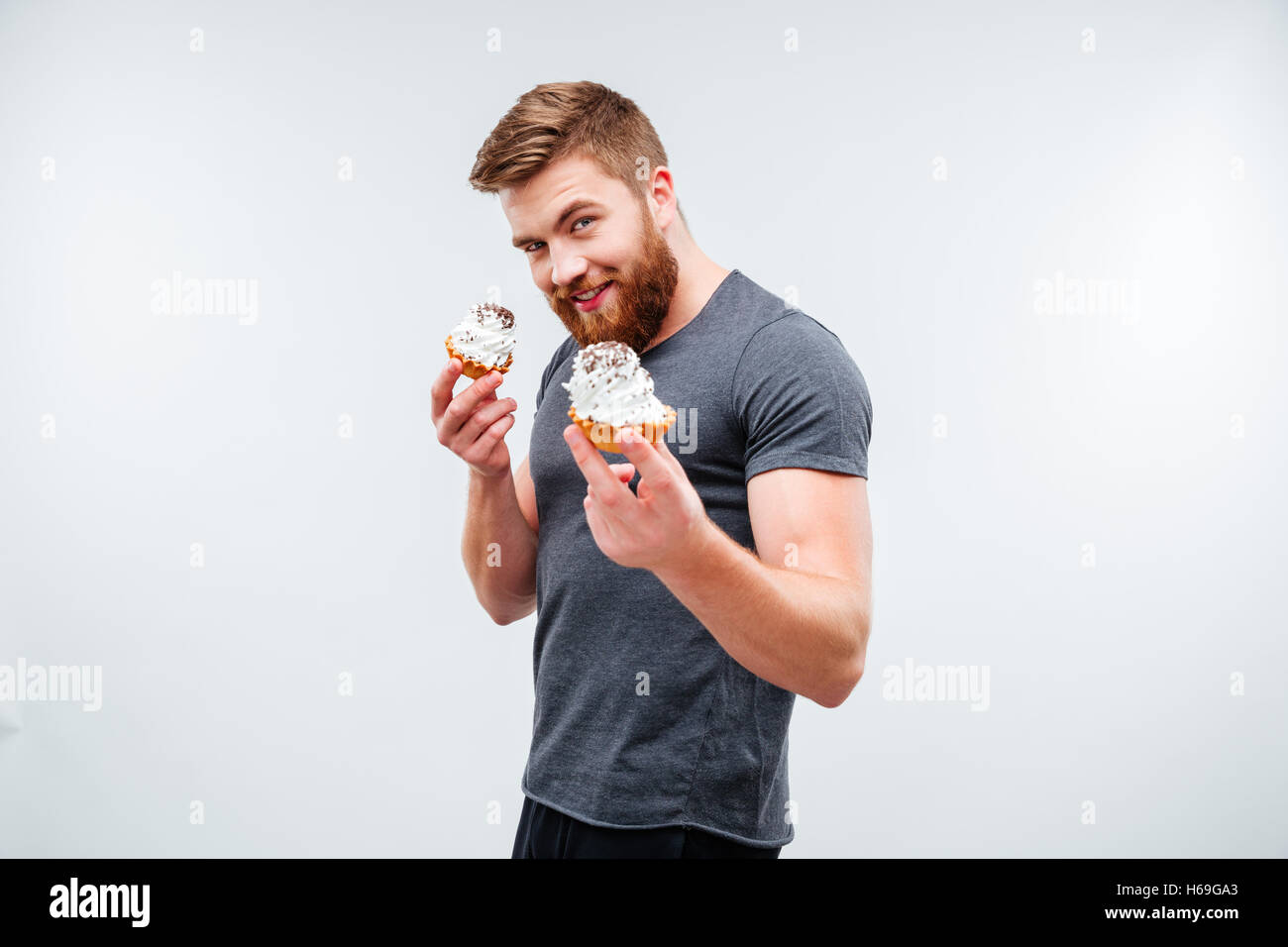 Happy bearded man holding two cream cakes isolated on white background ...