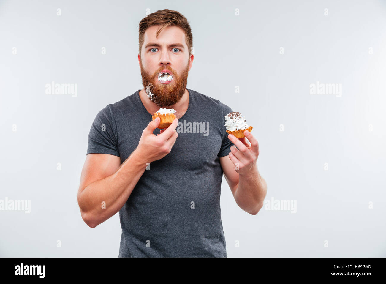 Filthy bearded young man eating cream cakes isolated on white ...