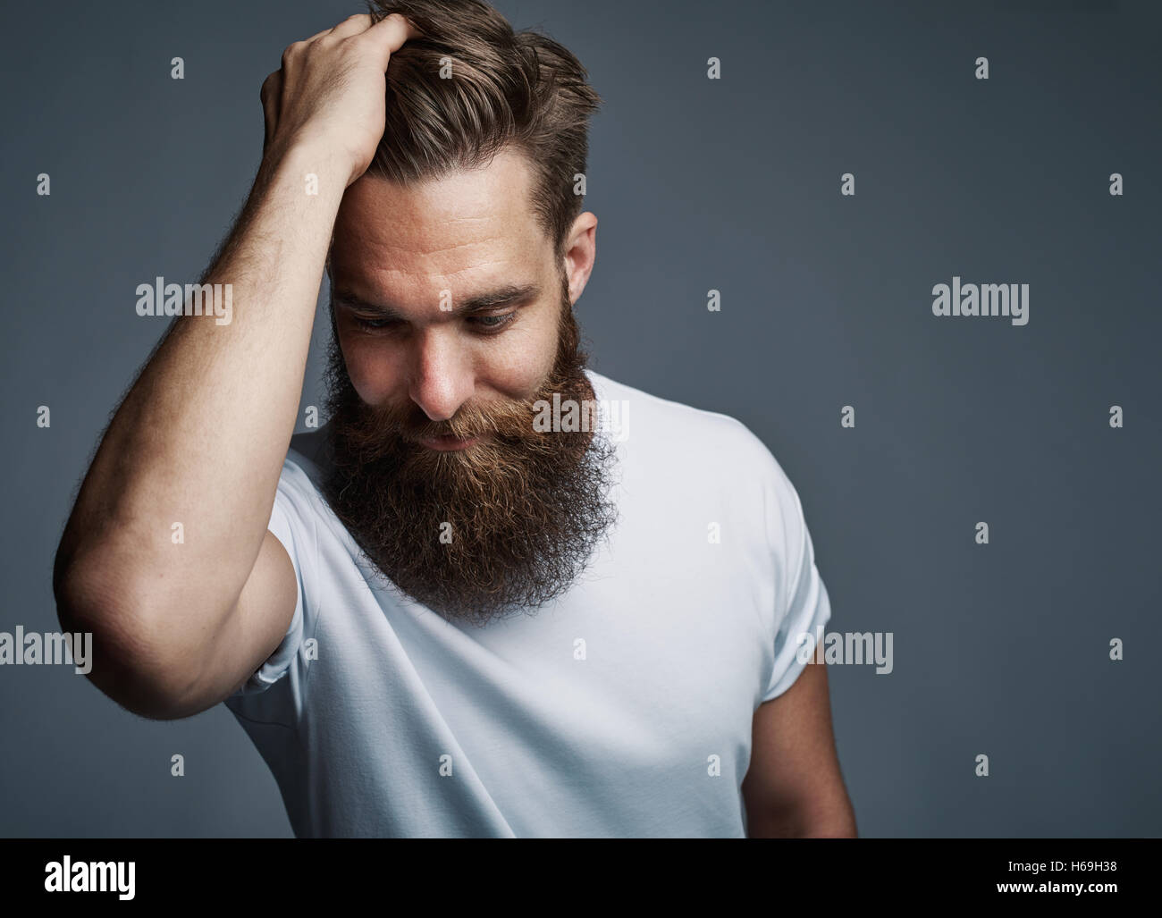 Thinking young man with long beard and white shirt holding hair while ...