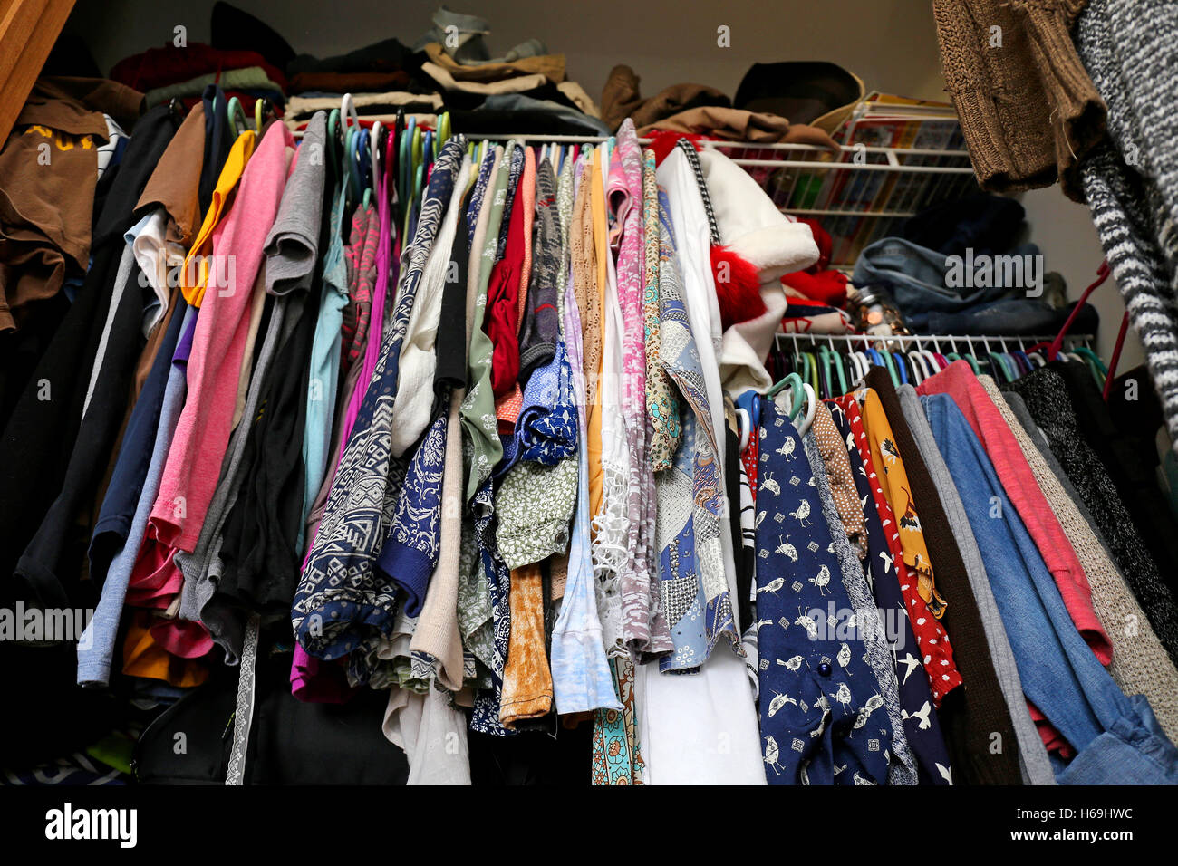 A messy young women's closet is fill with many outfits of colorful ...