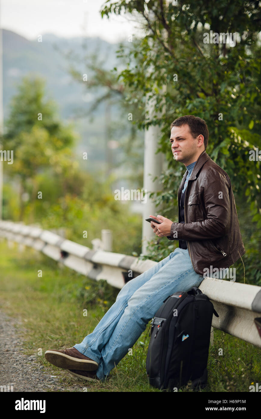 Man sitting on a road fence with gps tablet pc and using online maps ...