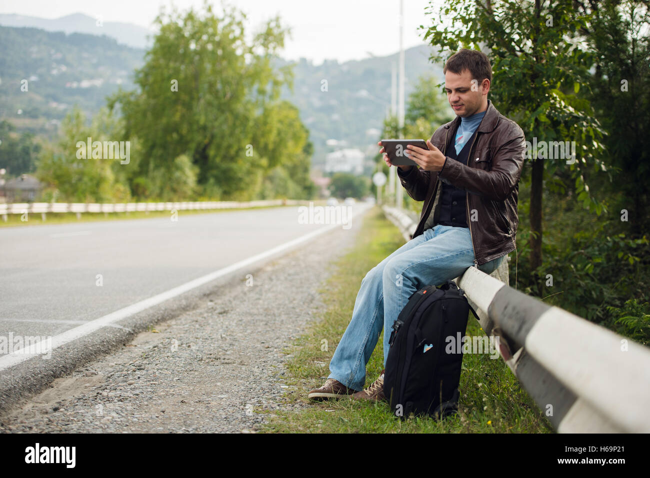 Man sitting on a road fence with gps tablet pc and using online maps ...
