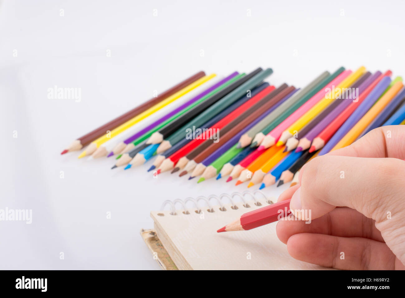 Hand holding a pencil beside the colorful pencils on a white background ...