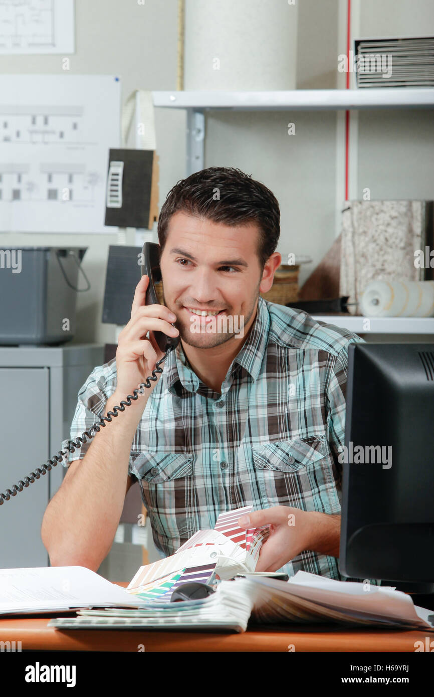 Man sat at desk, on telephone, holding color charts Stock Photo - Alamy