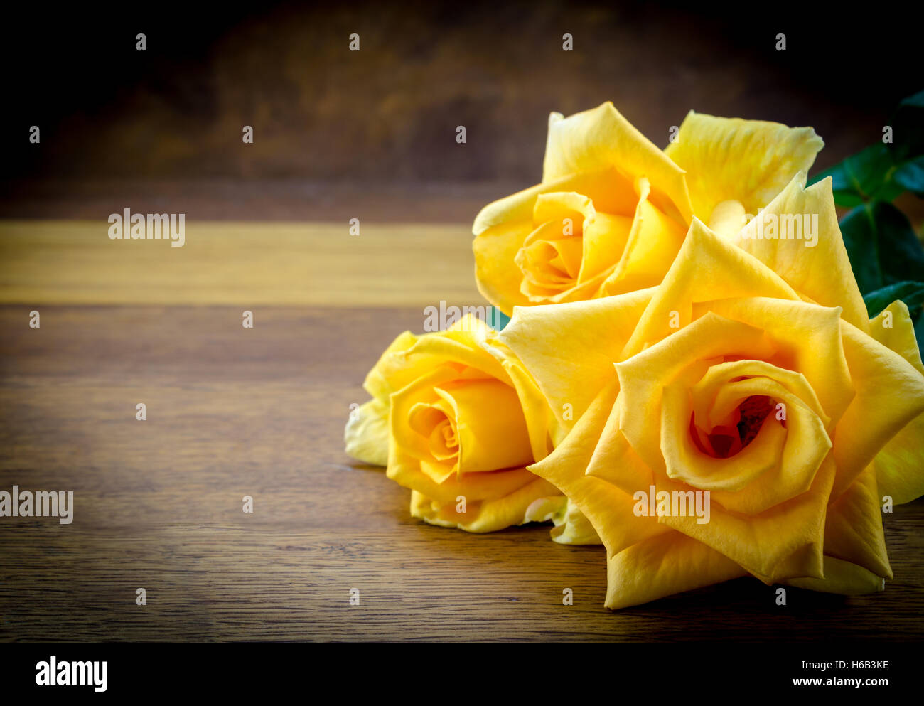 Photo of three yellow roses on wood table background Stock Photo - Alamy
