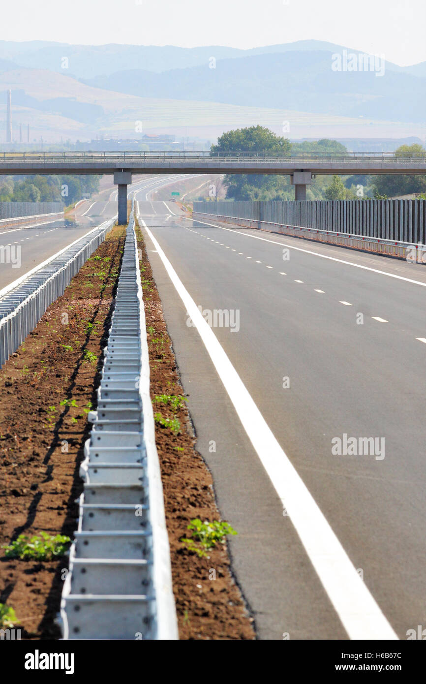 A vertical, image of an empty highway road and an overpass above it ...