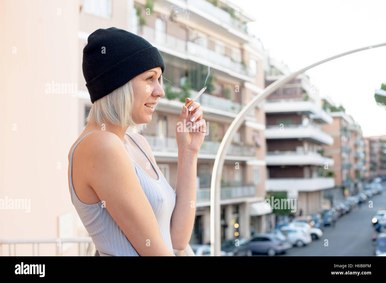 Young teen woman smoking cigarette and smiling outdoor with urban scene ...