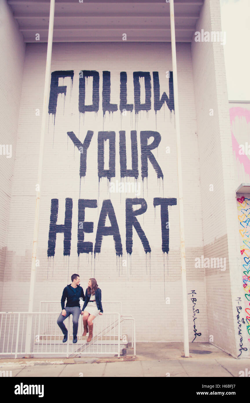 Couple sits in front of the Follow your heart wall at Union Market in ...