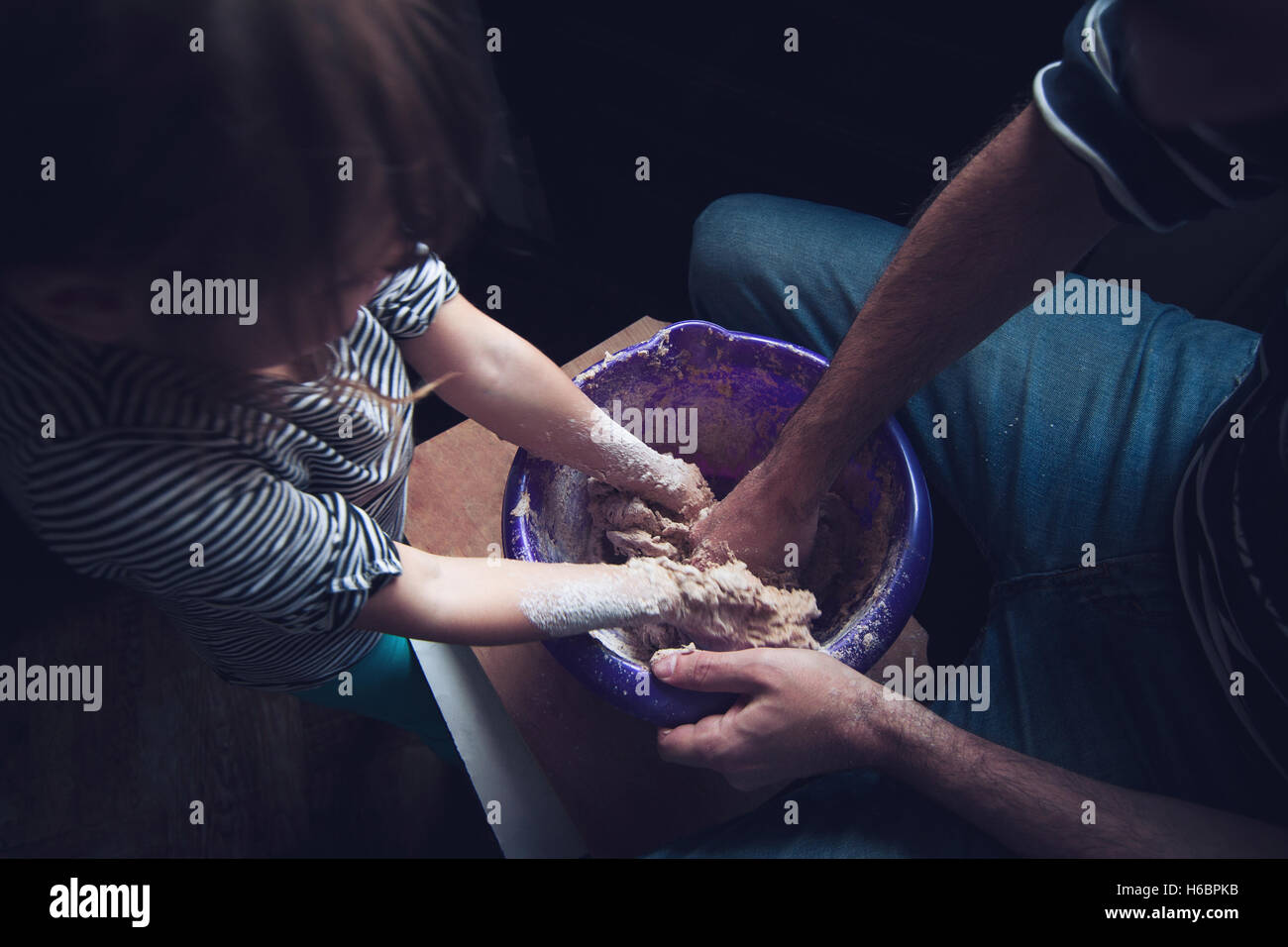 Top view of father and daughter working the dough of a bread together ...