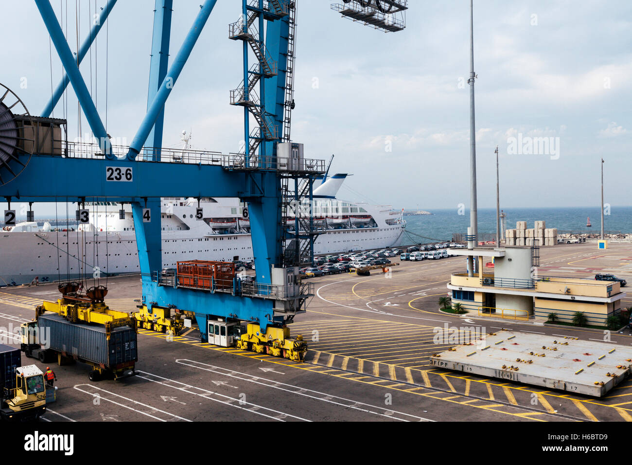 View of a freight dock with massive crane in a commercial harbor, with passenger ship in the ...