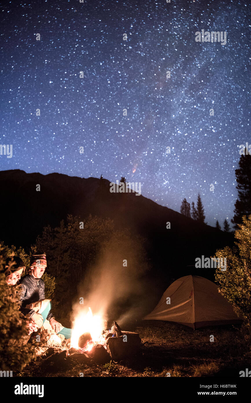 Two campers, a male and female, enjoying the warmth of the campfire on ...