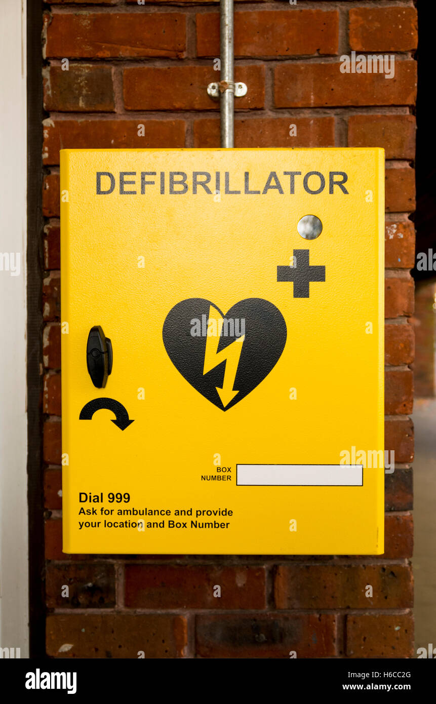 Yellow defibrillator box on an external brick wall of a shopping centre ...