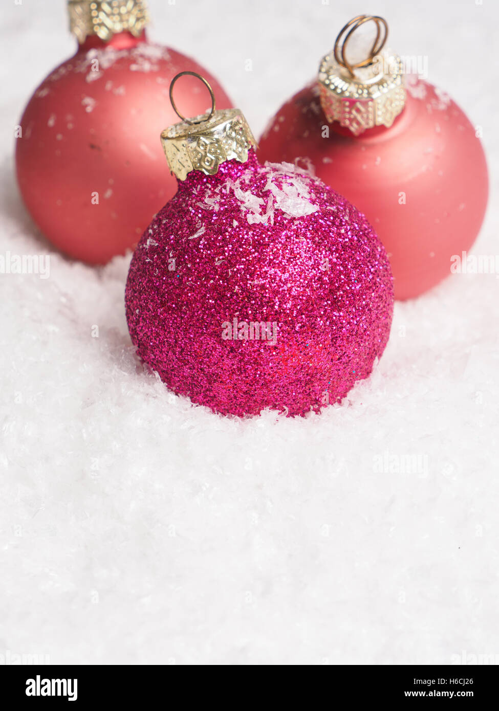 Three pink Christmas baubles on a snow background with space for text ...