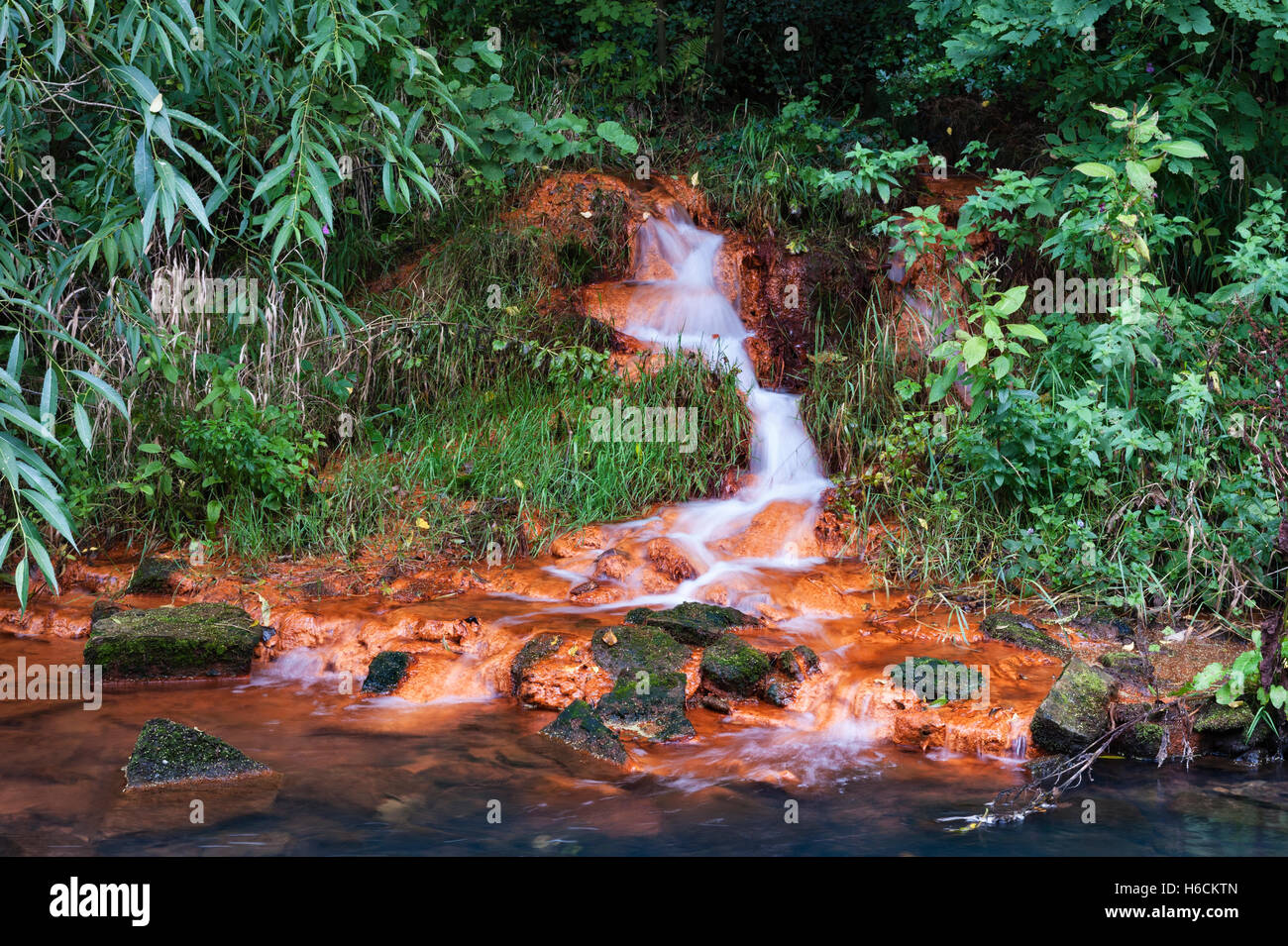 Bishop Auckland, County Durham, UK. A stream flowing over iron-rich red ...