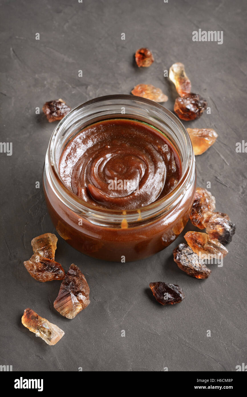 Homemade caramel in glass jar and caramelized sugar on black concrete ...