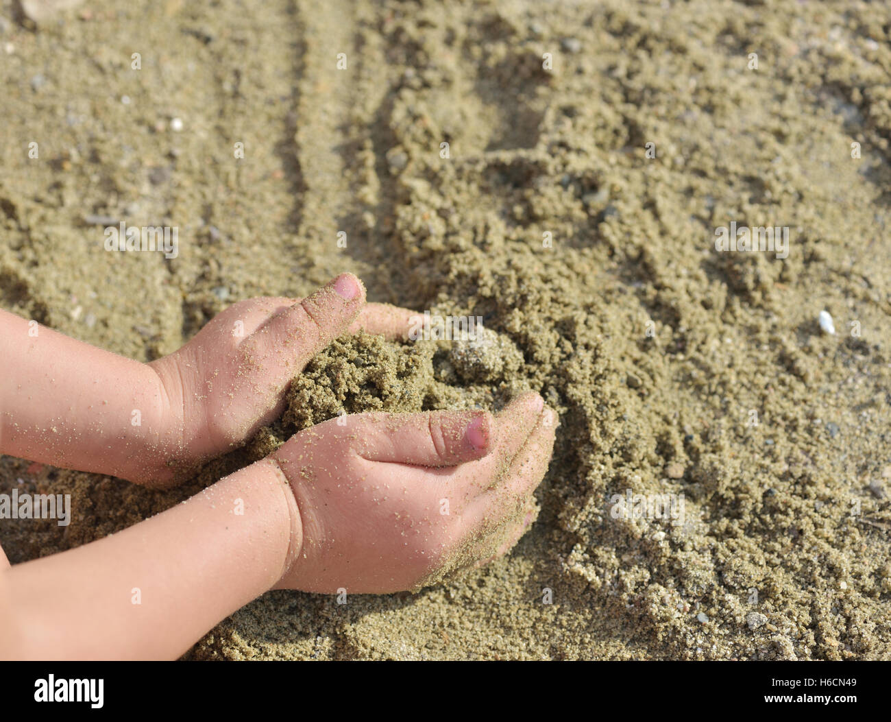 Kid playing with sand on a beach at sunset, starting to build a castle ...