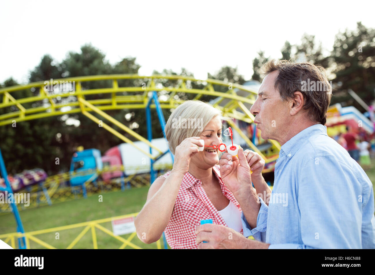 Senior couple having a good time at the fun fair, blowing soap bubbles ...