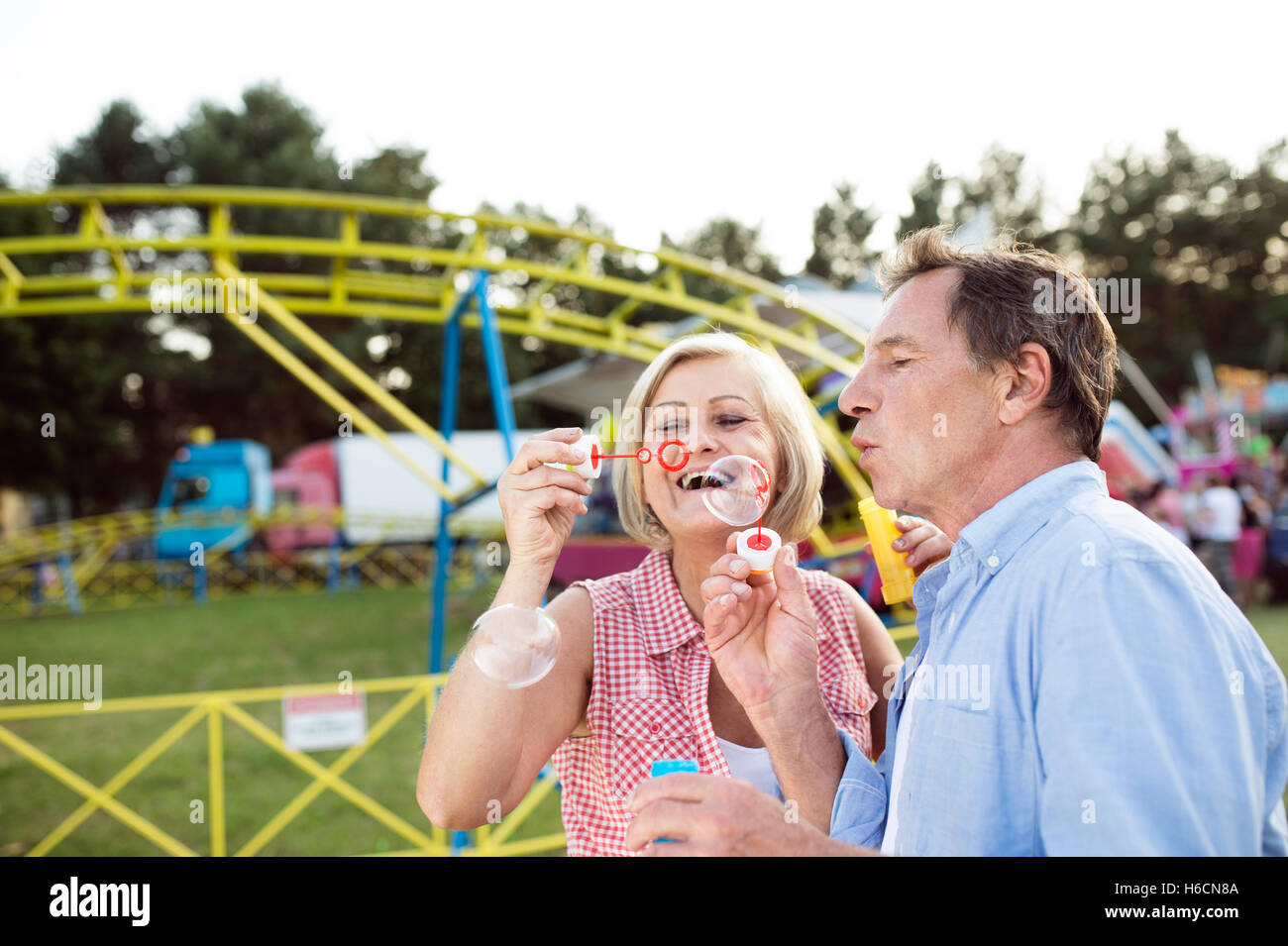 Senior couple having a good time at the fun fair, blowing soap bubbles ...