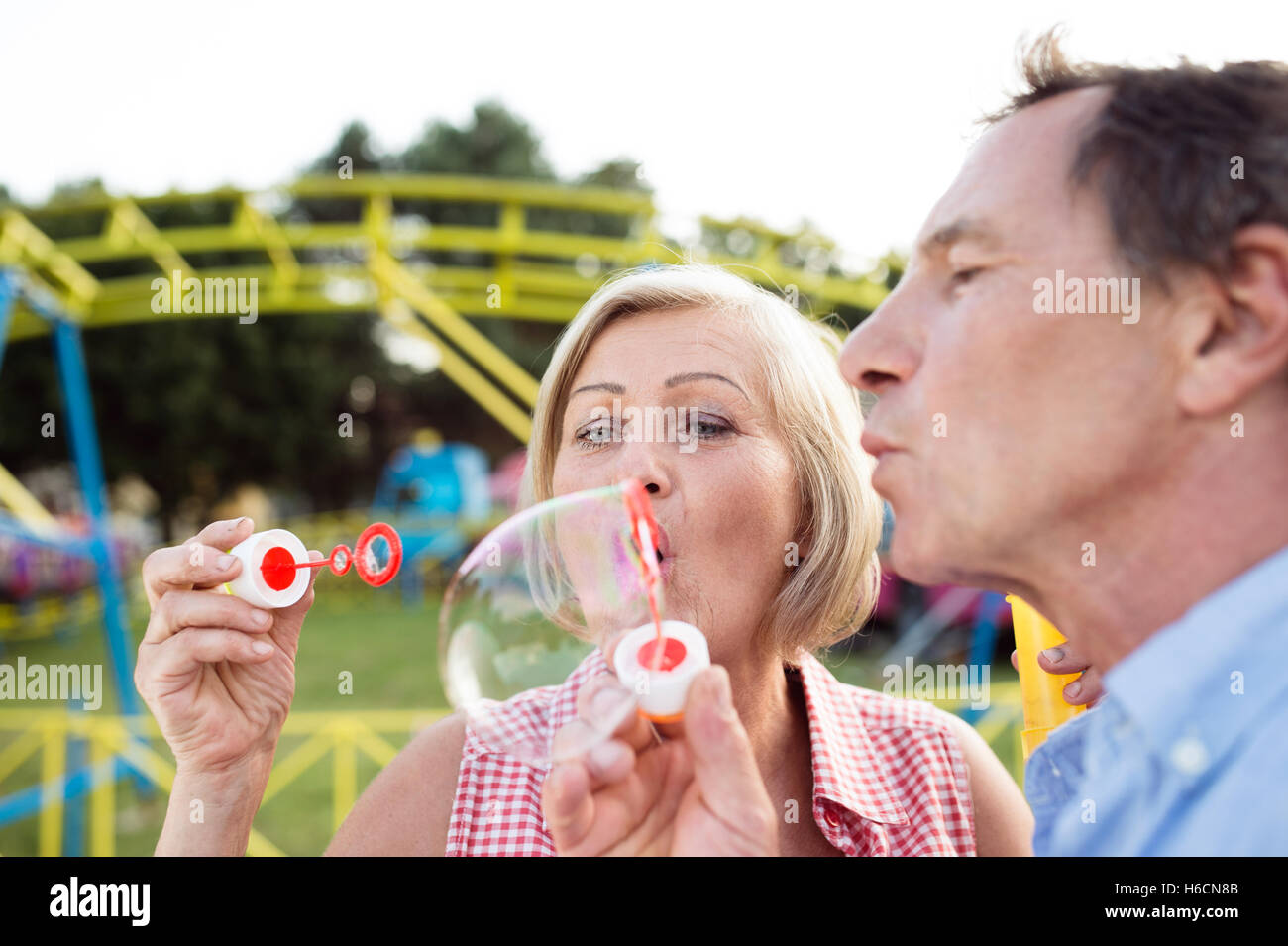 Senior couple having a good time at the fun fair, blowing soap bubbles ...