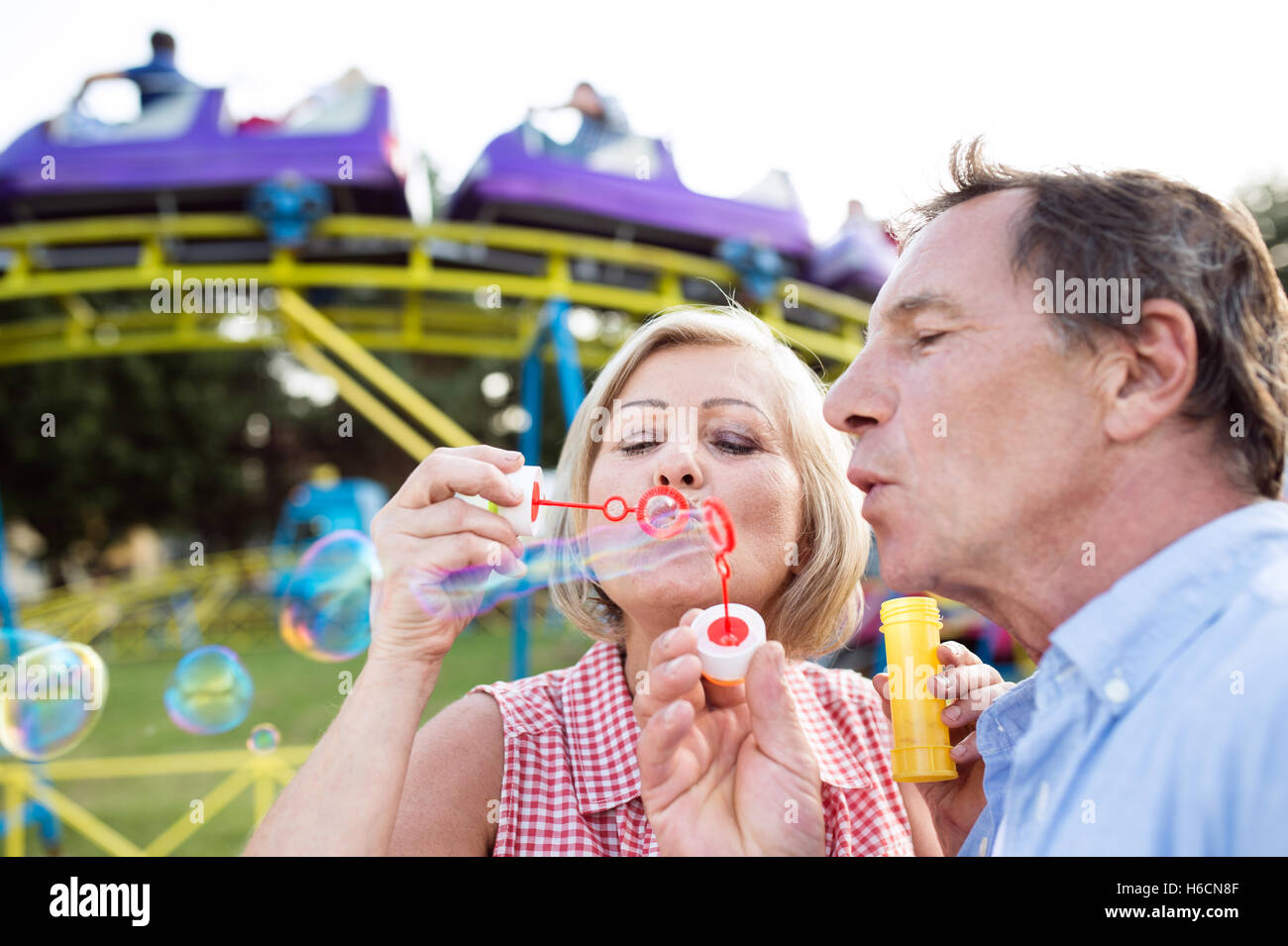 Senior couple having a good time at the fun fair, blowing soap bubbles ...