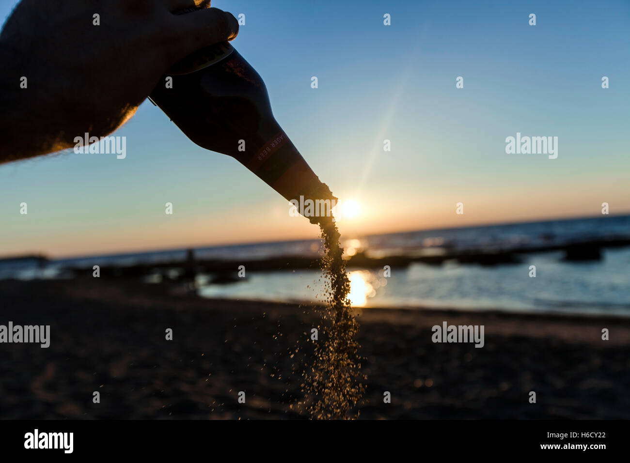 Silhouette of a hand holding a beer bottle with sand spilling out of it ...