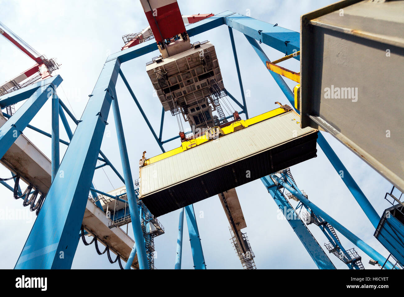 A massive freight crane transports a container from a truck onto a ...
