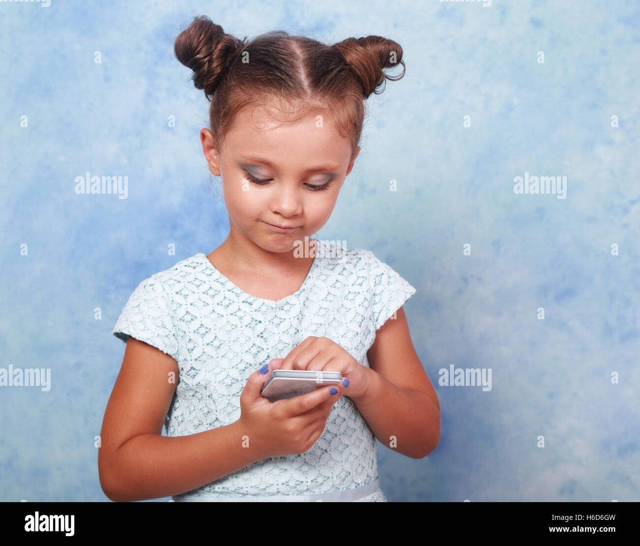 Cute kid girl with happy smile texting sms on mobile phone on blue ...