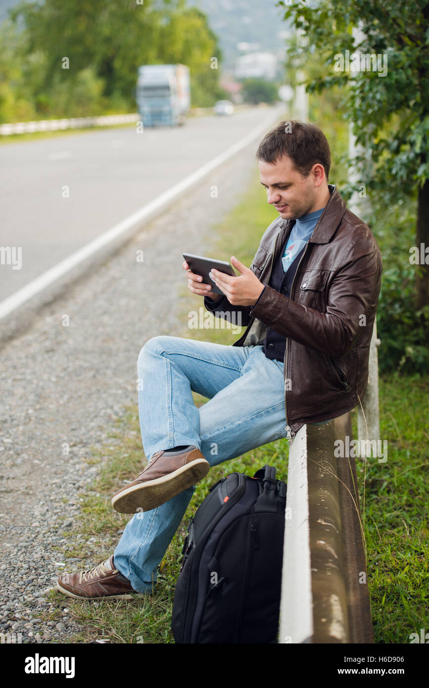 Man sitting on a road fence with gps tablet pc and using online maps ...
