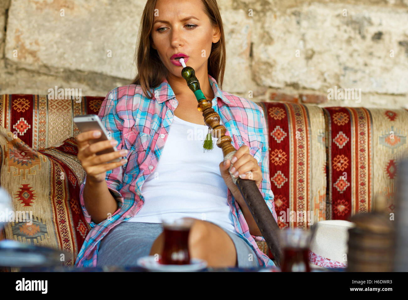 Beautiful young woman smoking a hookah and using smartphone in a cafe ...