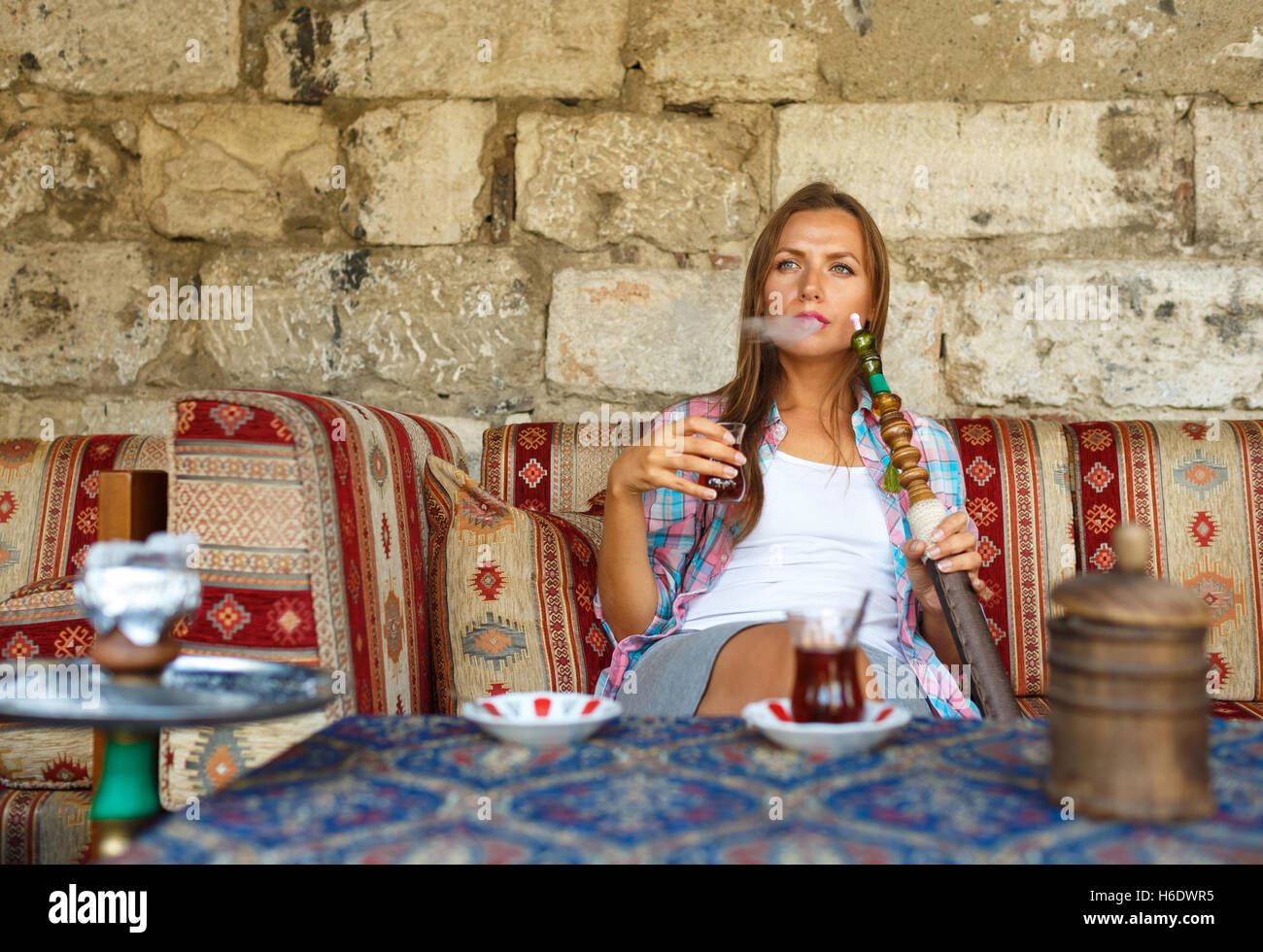 Beautiful young woman smoking a hookah and drinking tea in a cafe ...