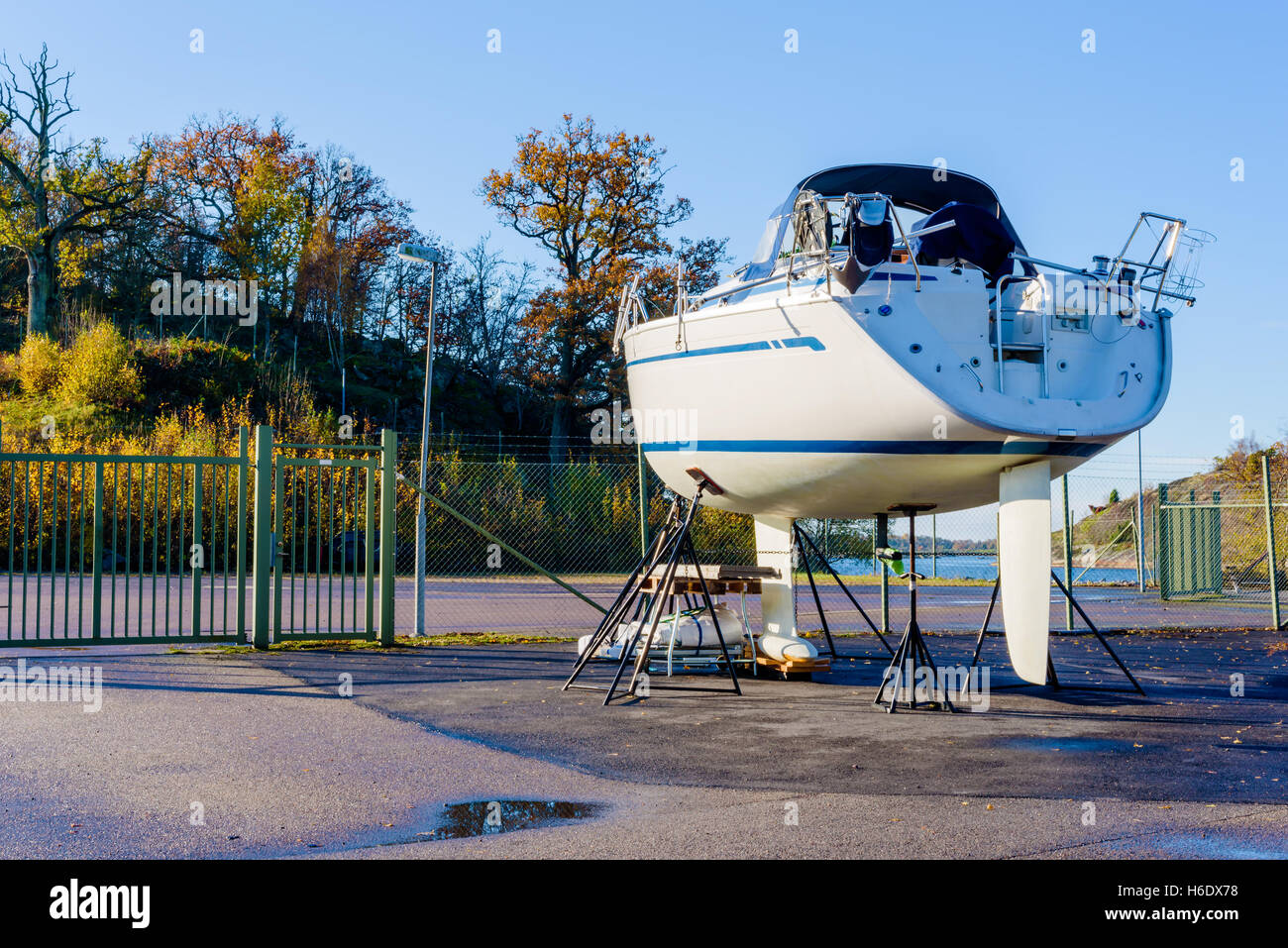 Sailboat on stilts outside fenced area in port in fall Stock Photo - Alamy