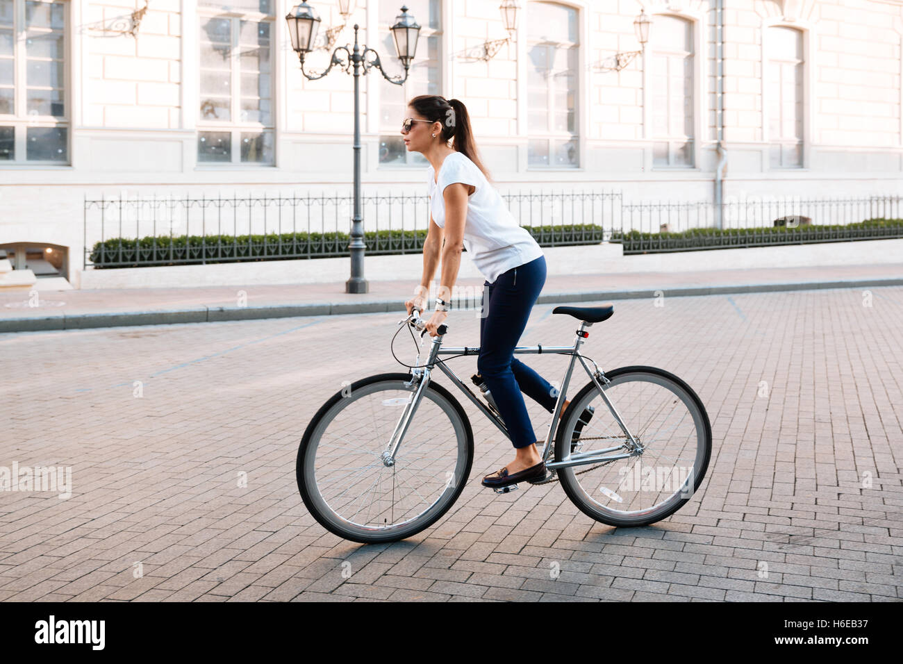 Side view portrait of a young beautiful woman riding on bicycle in city ...